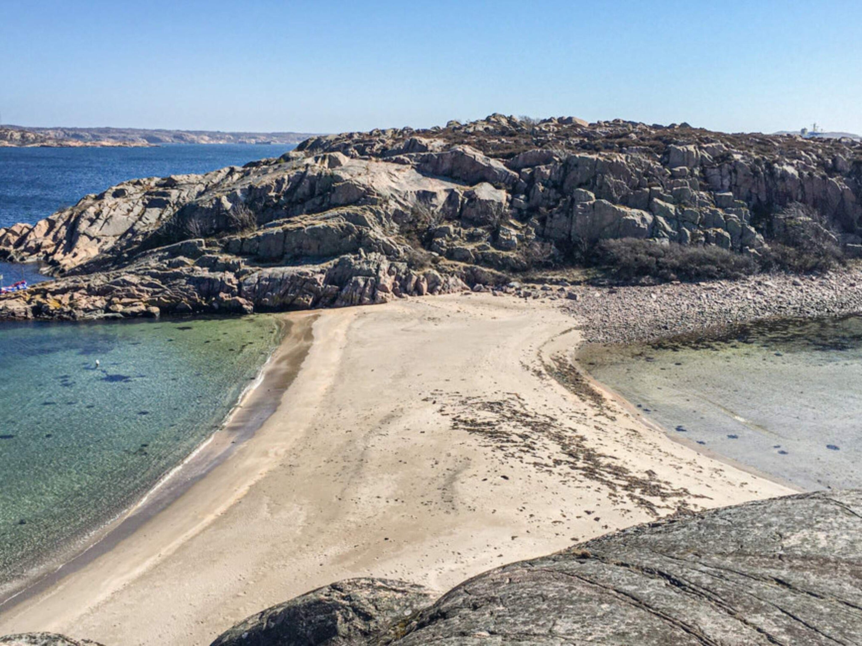 Uma praia rochosa com águas cristalinas e um caminho de areia que leva ao mar.