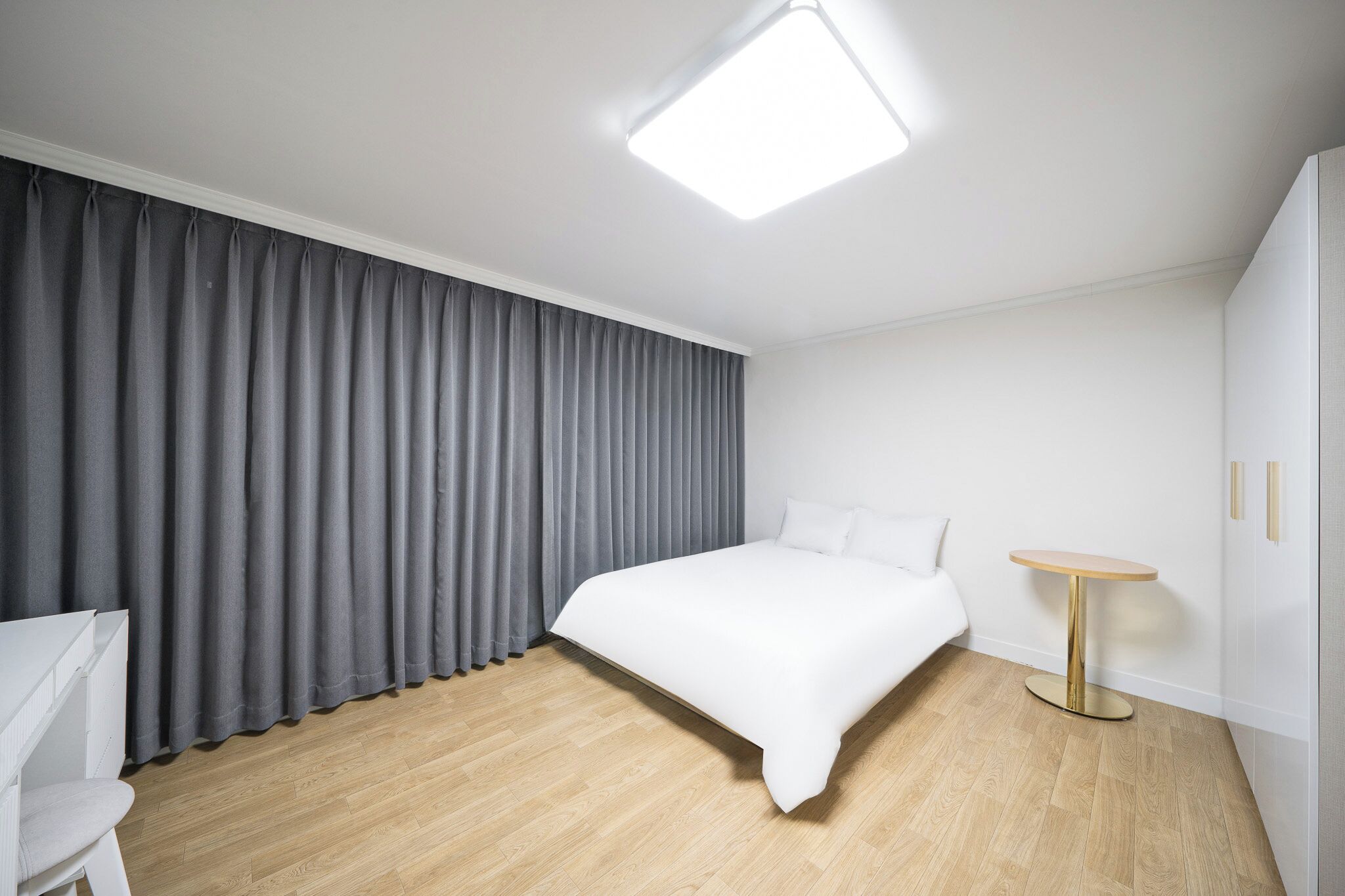 Quarto de hotel moderno com uma cama grande, uma mesa redonda pequena e uma luminária de teto iluminada.