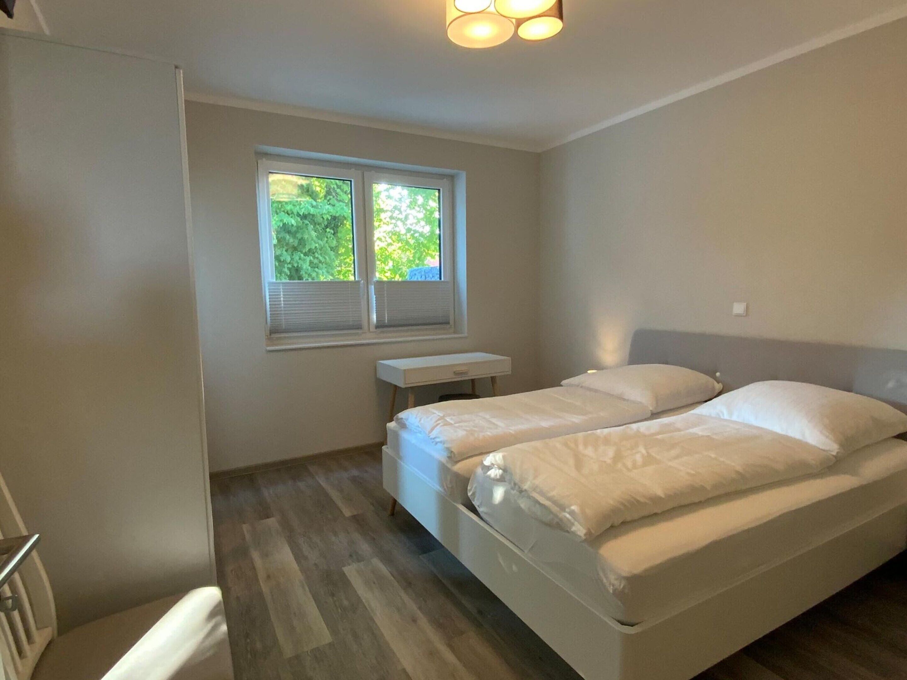 Quarto com duas camas, uma escrivaninha e janela com persianas.
