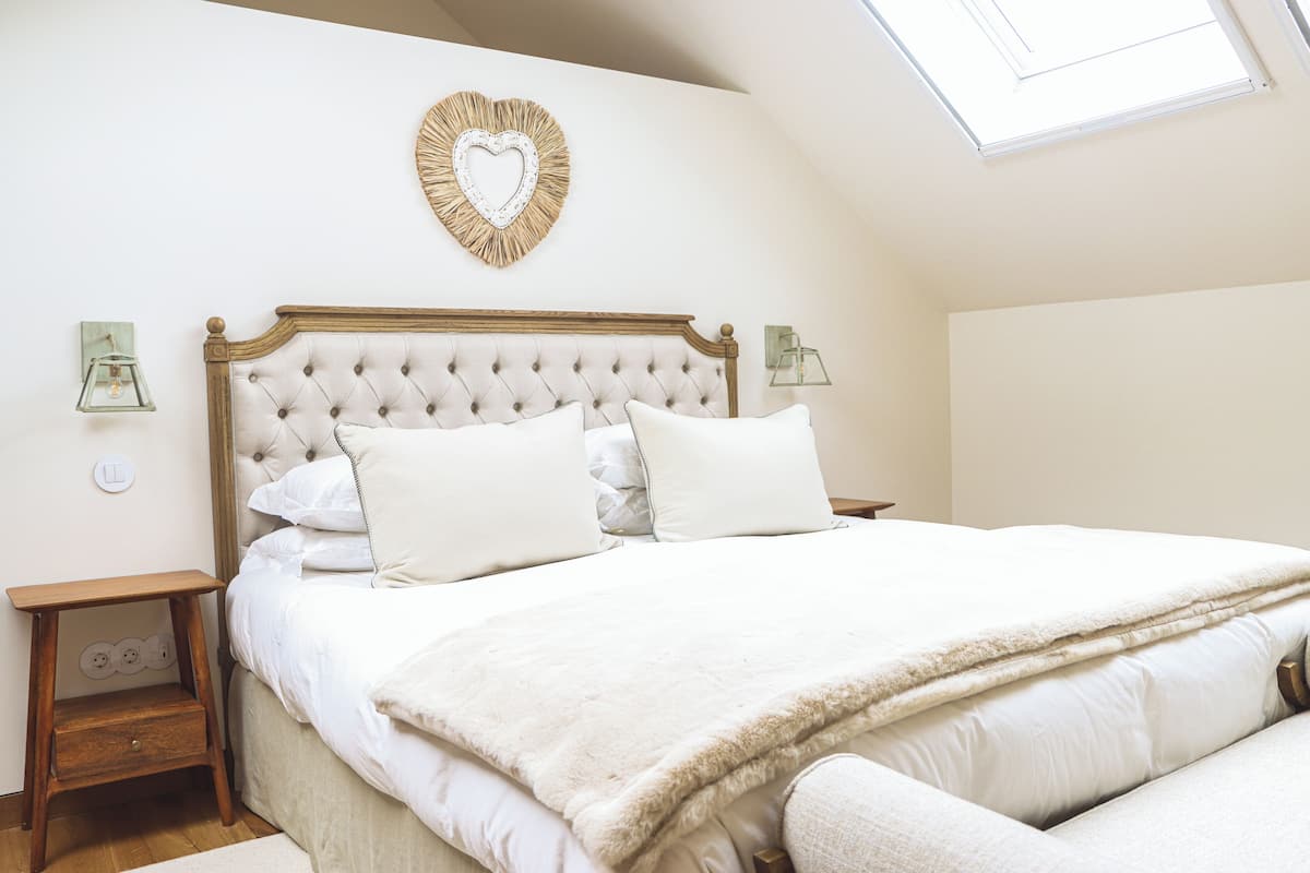 Quarto com cabeceira estofada, roupa de cama branca, decoração de parede em formato de coração e um claraboia.