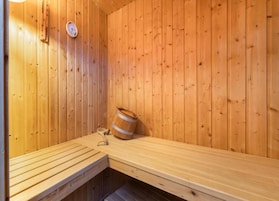 Uma sauna de madeira com um banco, um balde de madeira e um relógio na parede.