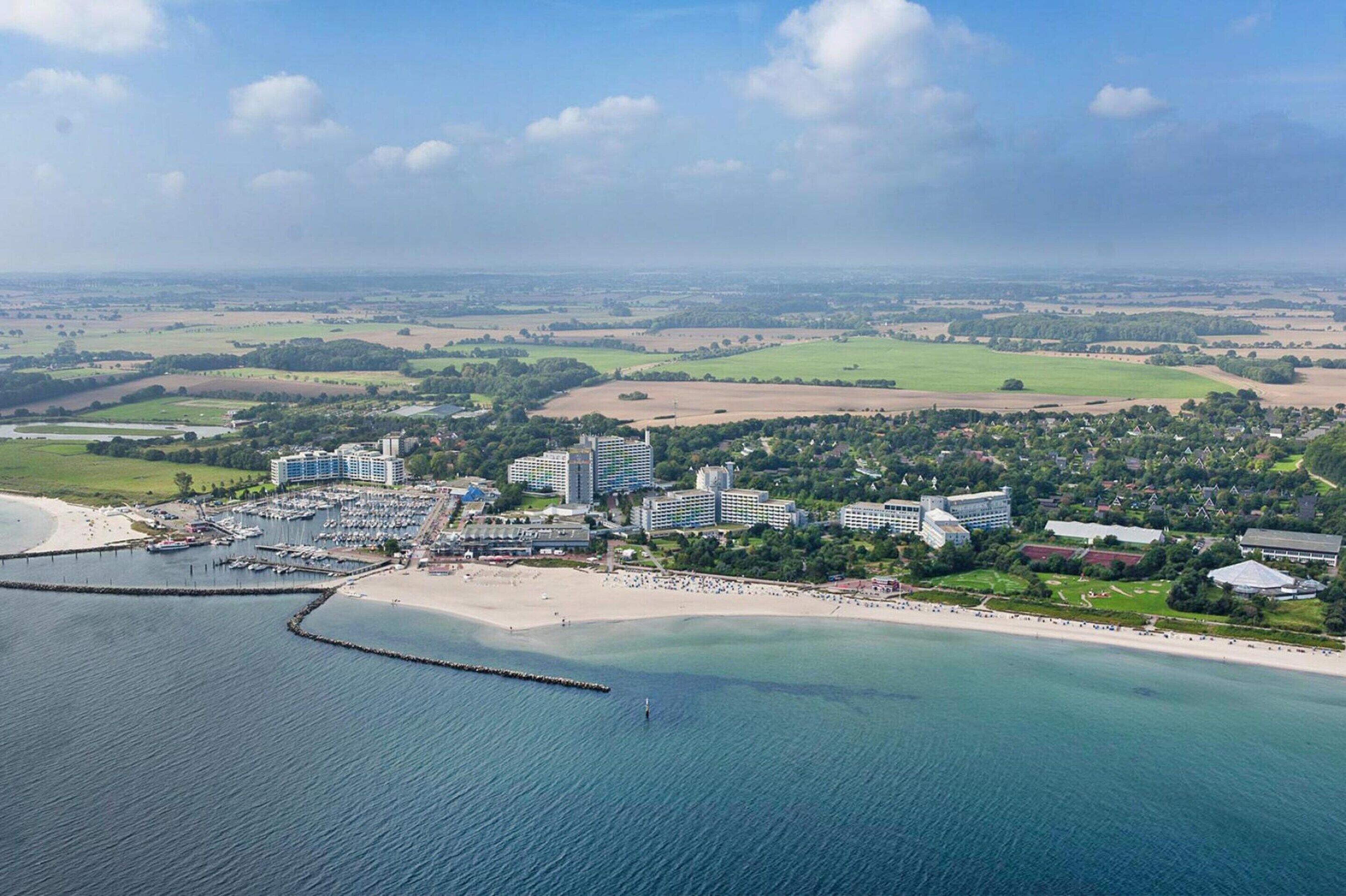 Vista aérea de um resort costeiro com vários edifícios de hotel, um porto de iates e uma praia.