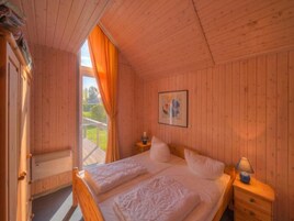Quarto com painéis de madeira, uma cama, mesa de cabeceira, luminária e janela com cortinas.