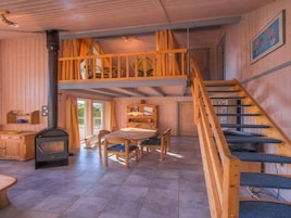 Interior acolhedor de uma cabana com área de jantar, escada de madeira e lareira.