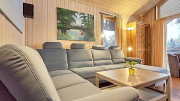 Uma sala de estar moderna com um sofá seccional, uma mesa de centro e um quadro de uma paisagem fluvial.