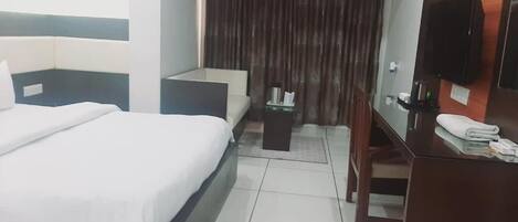 Quarto de hotel com uma cama, uma mesinha, uma televisão e um espelho.