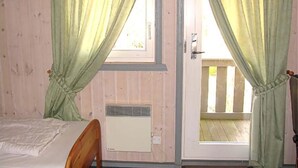 Quarto com cama, janela com cortinas e porta que dá para área externa.