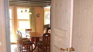 Uma sala de jantar com mesa e cadeiras de madeira, luminária pendente e porta com puxador de latão.