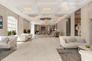 Um hall de hotel espaçoso com piso de mármore, dois sofás, um balcão de recepção e um lustre.