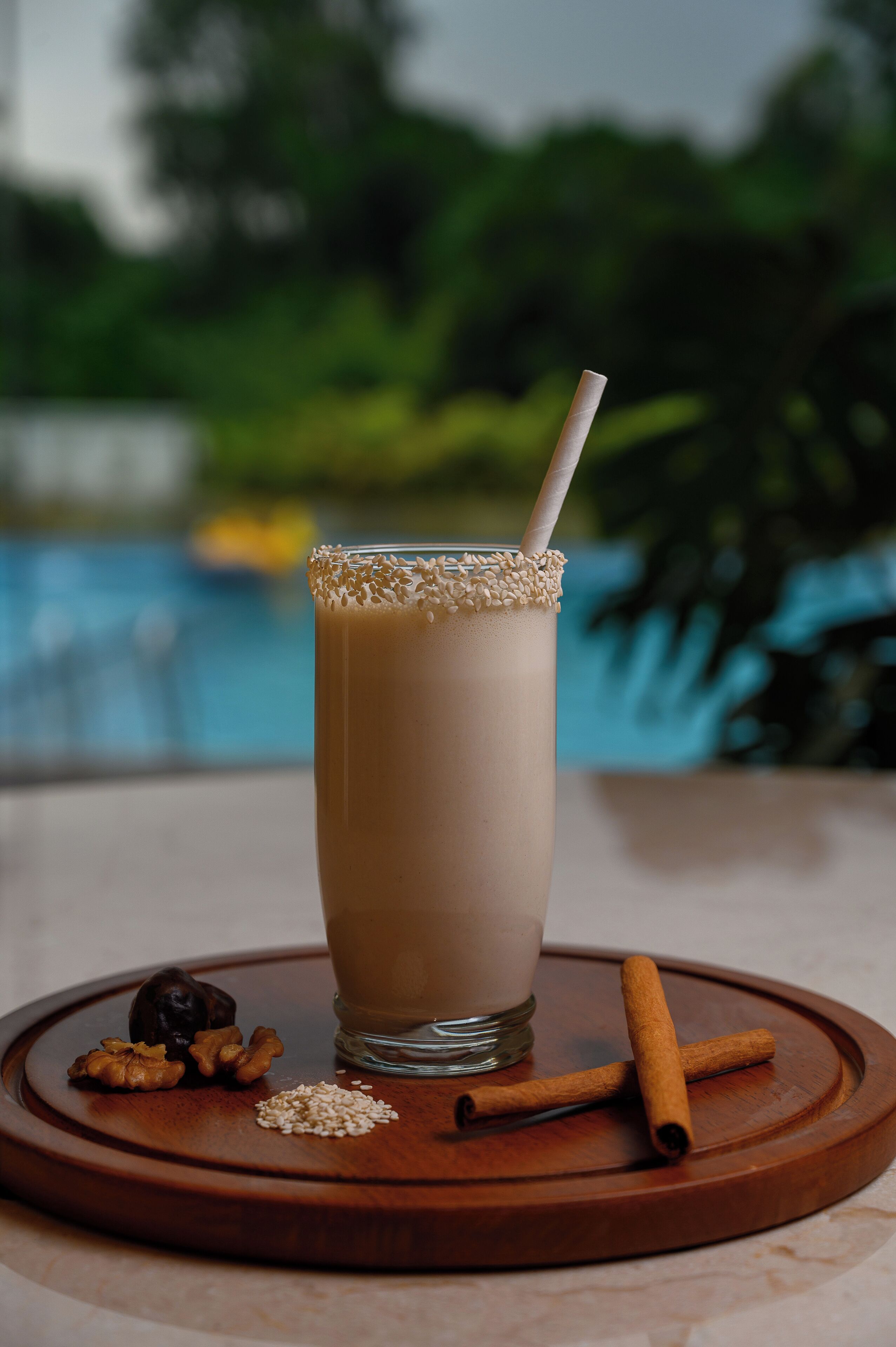 Um copo de café gelado com canudo, cercado por nozes e paus de canela em um tabuleiro de madeira.