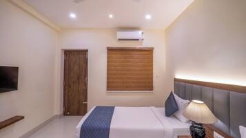 Quarto de hotel com cama, luminária, ar condicionado e televisão na parede.