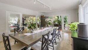 Uma sala de jantar espaçosa com uma mesa comprida, cadeiras pretas e plantas em vasos.