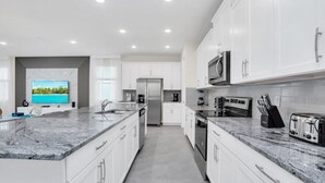 Cozinha moderna com armários brancos, bancadas de granito, micro-ondas embutido e uma ilha grande com pia.
