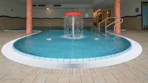 Piscina interna com um elemento central de água, rodeada por piso ladrilhado e colunas com desenhos padronizados.