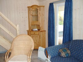 Um quarto com uma cadeira de vime, um sofá azul estampado, um armário de madeira com espelho e uma porta de vidro deslizante com cortinas azuis.