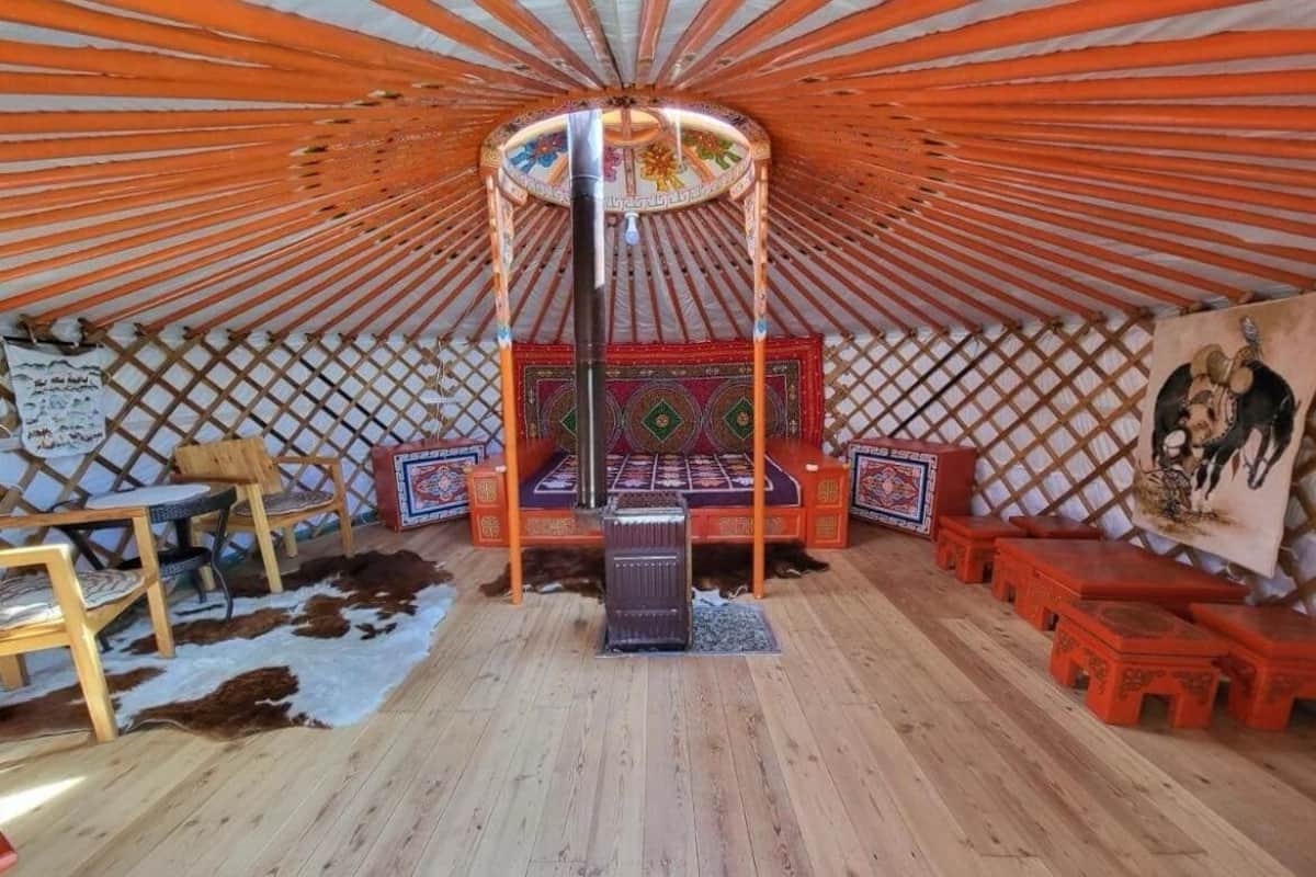 Interior de iurte tradicional, com cama central, mobiliário de madeira e decoração na parede.