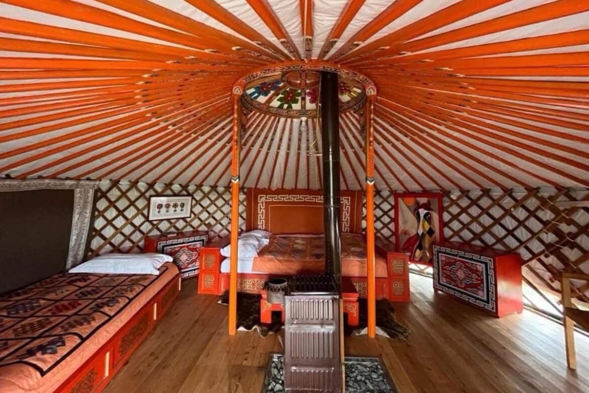 Interior de uma yurt tradicional, com uma cama central, piso de madeira e teto decorativo.