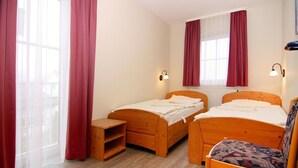 Quarto com duas camas de madeira, uma mesa de cabeceira de madeira, uma cadeira e uma janela com cortinas vermelhas.