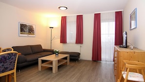 Uma sala de estar com sofá, mesa de centro, luminária, TV e escrivaninha de madeira com cadeira.