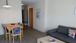 Uma sala de estar com sofá, mesa de centro, mesa de jantar com cadeiras e um corredor que dá para outro cômodo.
