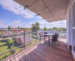 Um deck de madeira com mesa e cadeiras, com vista para uma área residencial com casas e vegetação.