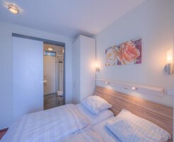 Quarto com duas camas, uma cabeceira de madeira, um quadro na parede e uma porta que dá para o banheiro.