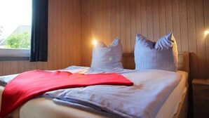 Um quarto com painéis de madeira, uma cama, almofadas e uma janela.