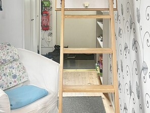 Quarto com escada de madeira, sofá branco e almofada azul, e parede estampada.