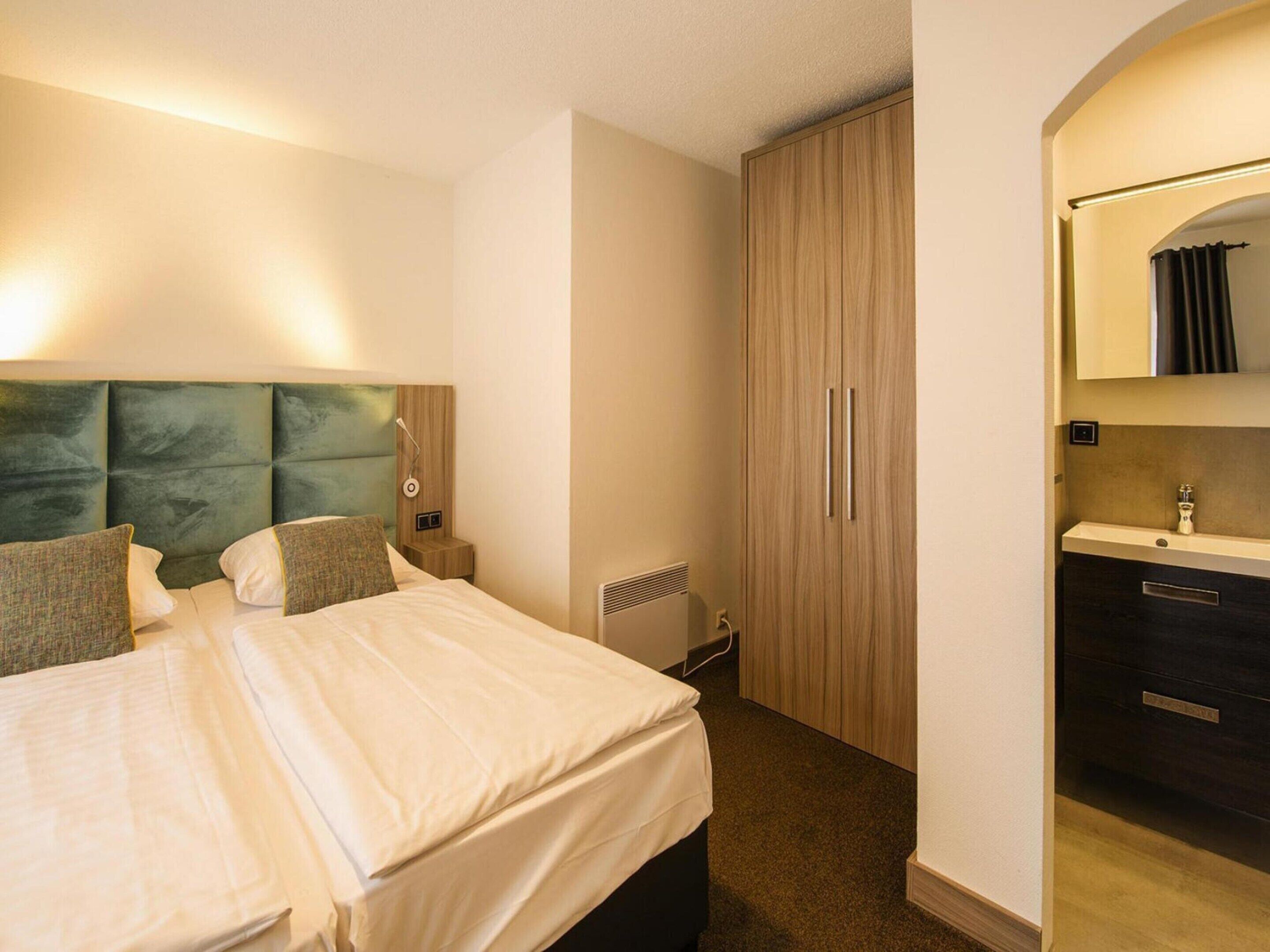 Quarto de hotel com cama, mesa de cabeceira, espelho, armário e banheiro.