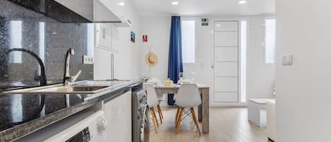 Cozinha moderna com máquina de lavar e secar integradas, sala de jantar com mesa e cadeiras, e vista para o quarto vizinho.