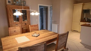 Uma área de refeições com uma mesa e cadeiras de madeira, um armário com portas de vidro e uma cozinha com armários e micro-ondas.