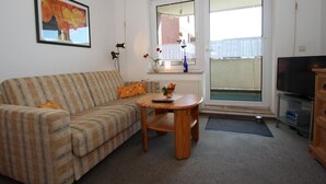 Uma sala de estar com um sofá listrado, uma mesa de centro de madeira, uma televisão e uma janela com cortina roxa.
