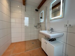 Casa de banho com azulejos brancos, uma pia, um espelho e um chuveiro.