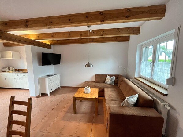 Sala de estar com teto de madeira, sofá, mesa de centro, televisão e janela com vista.