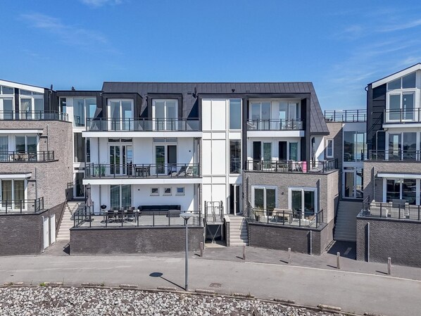 Um edifício residencial moderno, com várias andares, varandas, grandes janelas e um telhado plano.