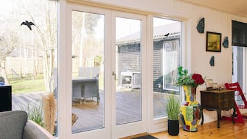 Quarto com porta de vidro deslizante para um deck exterior, uma cadeira preta, um vaso colorido com flores e uma mesa de madeira.