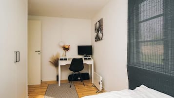 Quarto com cama, escrivaninha com computador, cadeira e janela com mosquiteiro.