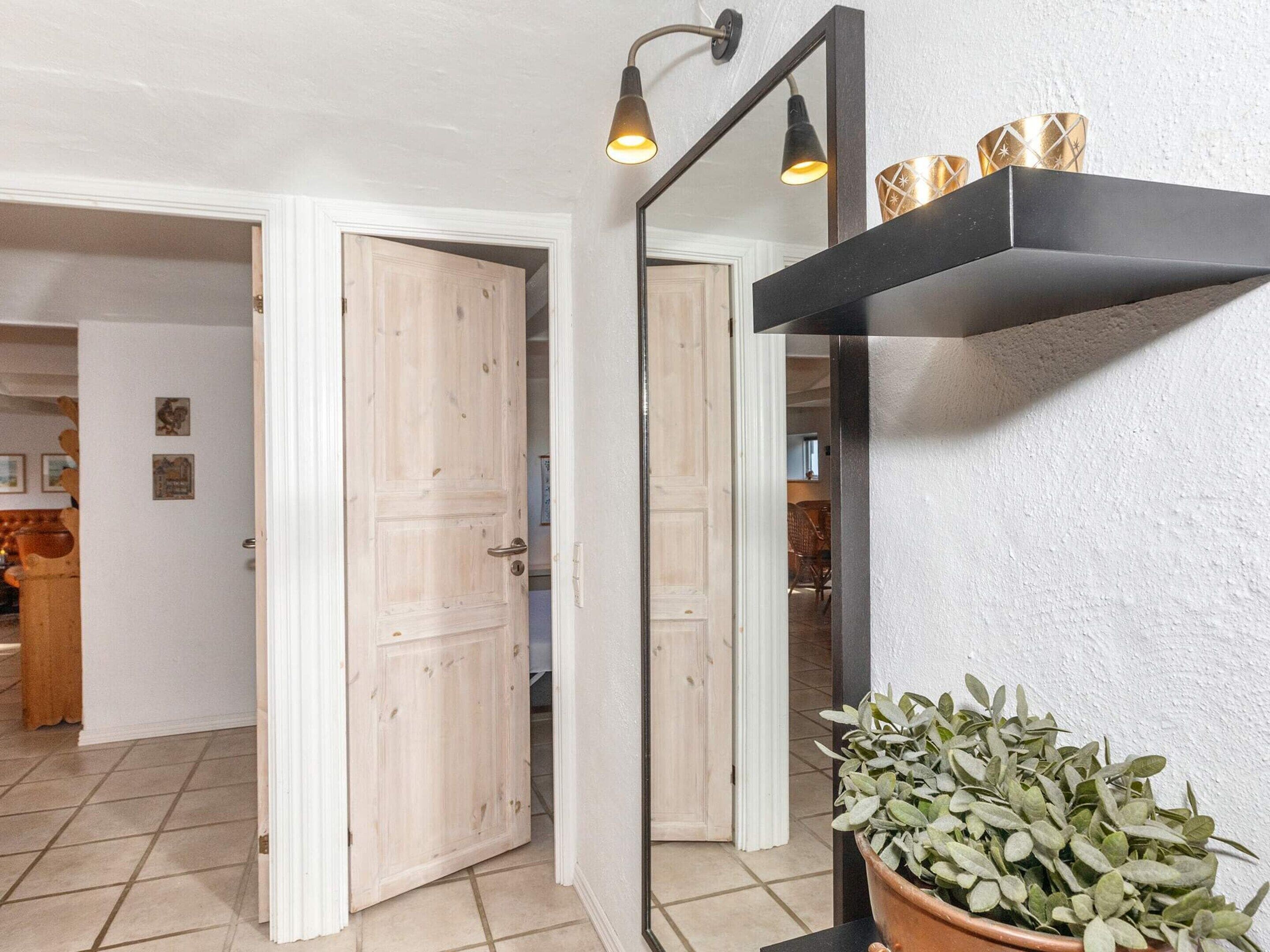 Um corredor com porta de madeira, planta em vaso e prateleira preta com objetos decorativos.