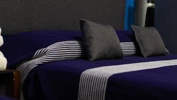 Cama bem arrumada com roupa de cama listrada e duas almofadas, cabeceira escura e um alto-falante ao fundo.