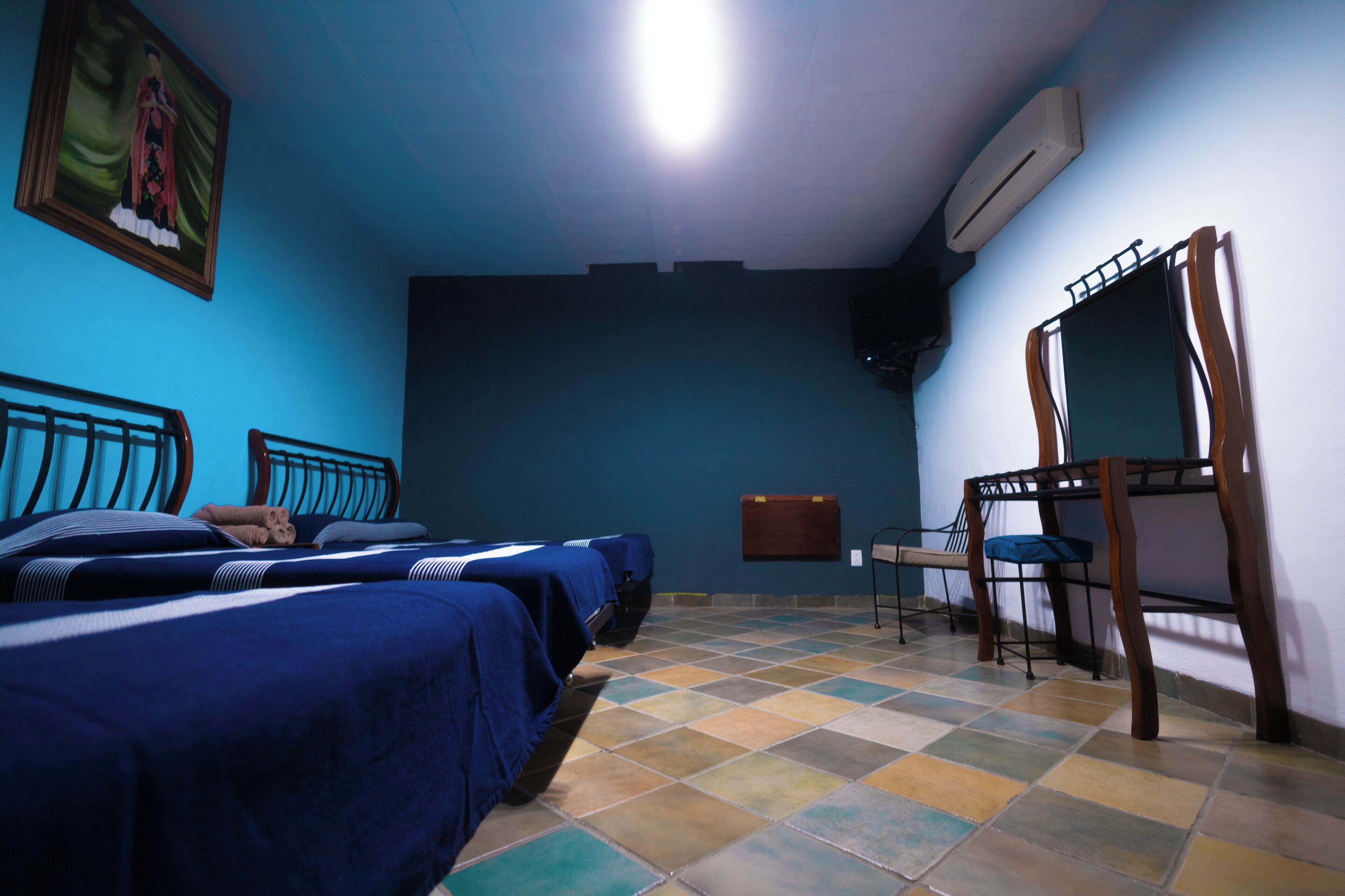 Quarto com duas camas, uma escrivaninha, uma cadeira e televisão na parede.
