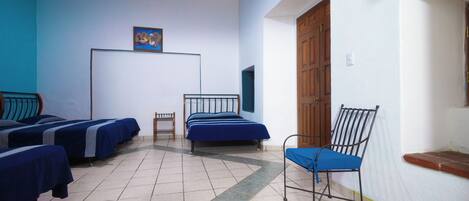 Quarto com três camas, uma cadeira, porta de madeira e um quadro na parede.