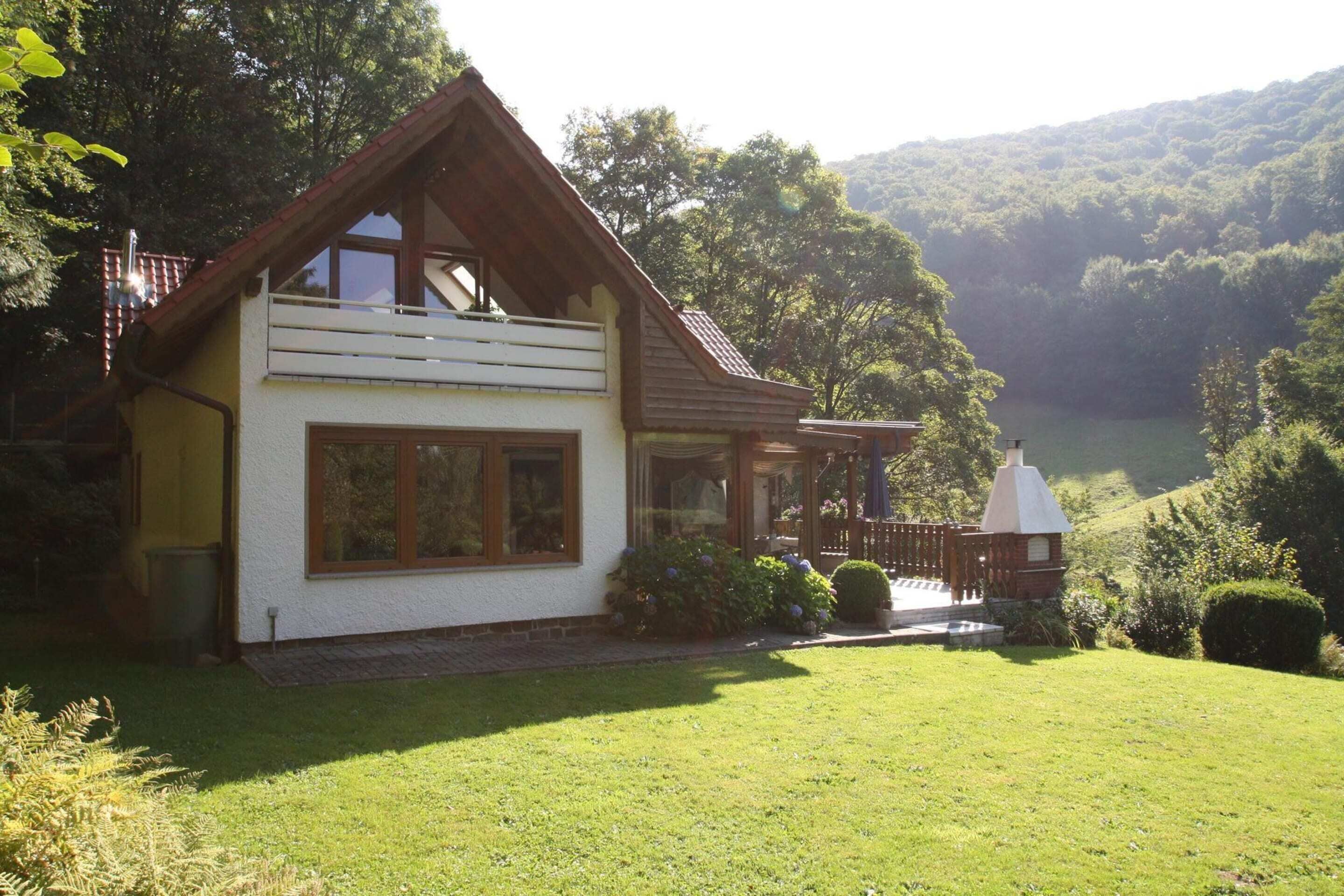 Uma casa de dois andares com varanda, cercada por vegetação exuberante e um lago.