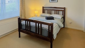 Um quarto com cama de madeira, janela com persianas, abajur e luminária no teto.