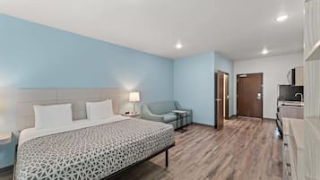Quarto de hotel moderno com cama grande, escrivaninha, cadeira e cozinha compacta.