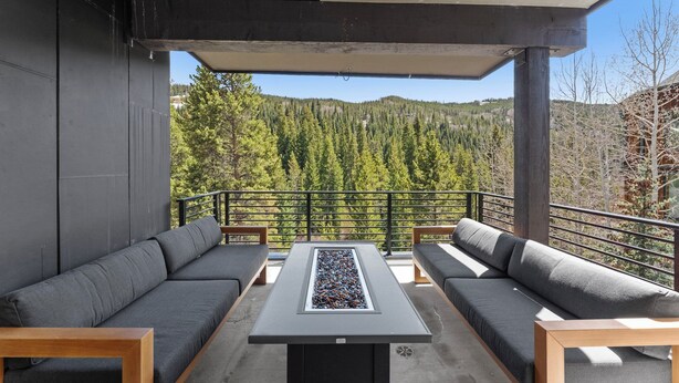 Varanda com sofá e mesa, com vista para uma montanha arborizada.