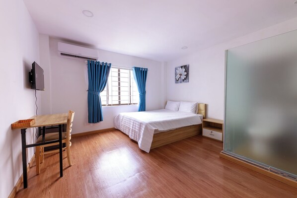 Quarto com cama, escrivaninha, cadeira, televisão e janela com cortinas.