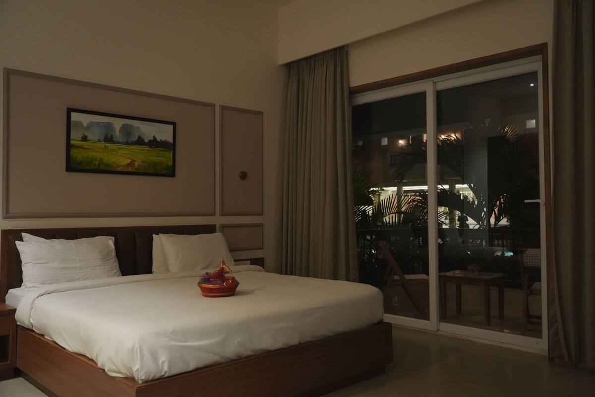 Quarto de hotel com uma cama grande, um quadro na parede e vista através de uma porta de vidro deslizante.