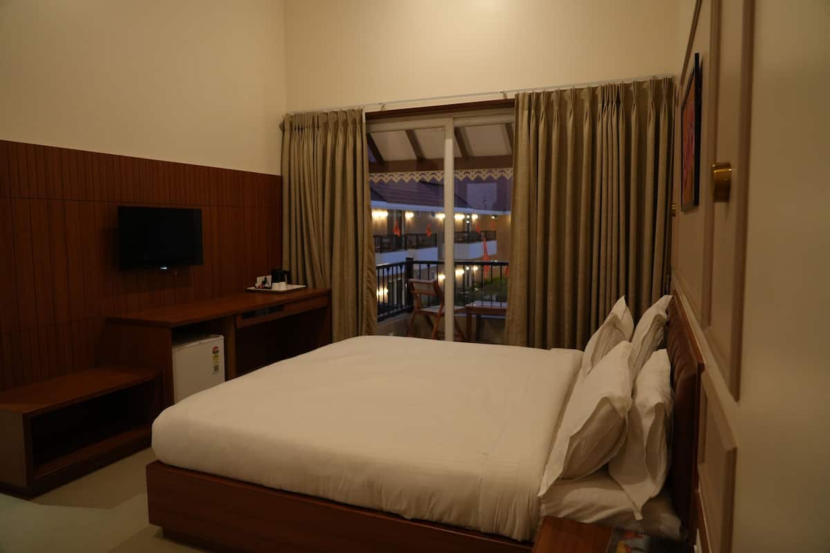 Quarto de hotel com cama, escrivaninha, televisão e varanda com cortinas.