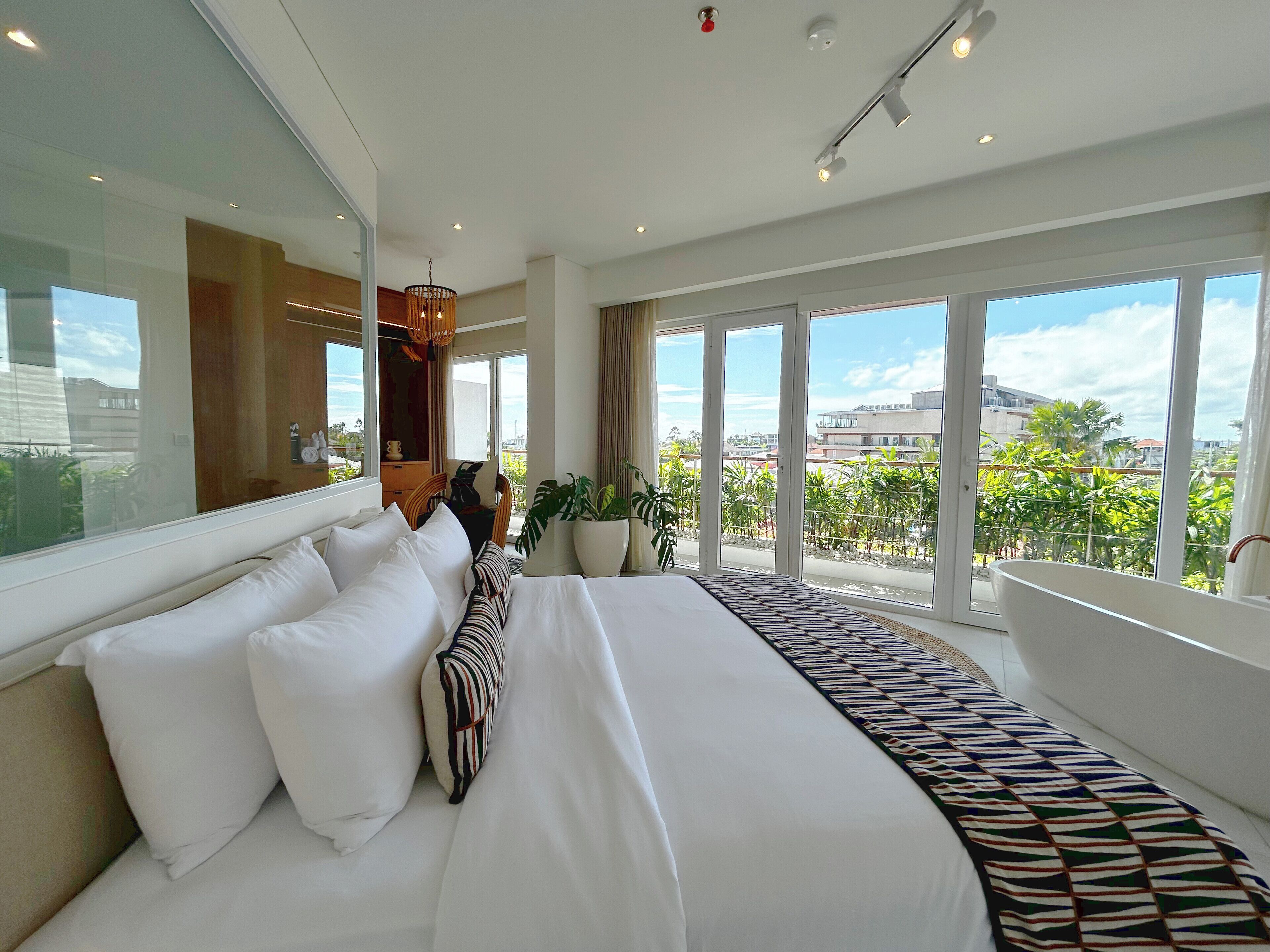 Quarto espaçoso com uma cama grande, vista da cidade e uma varanda com plantas.