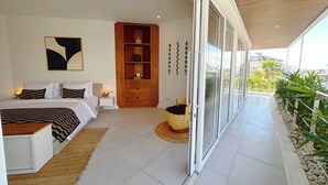 Quarto moderno com uma cama grande, um guarda-roupa de madeira, um pequeno espaço de estar e uma varanda com plantas.